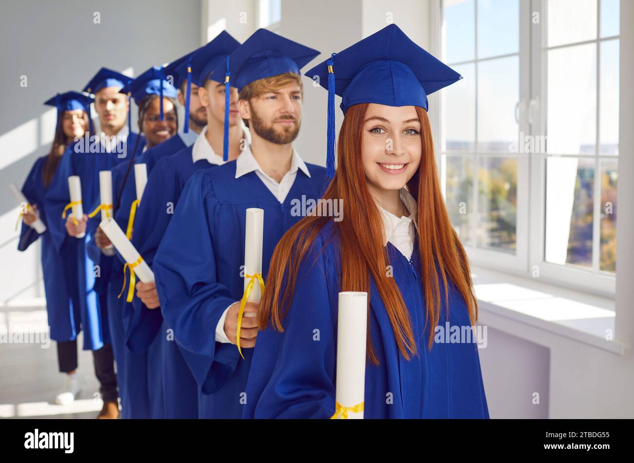 Young happy graduates standing indoors in a row at graduation ceremony ...