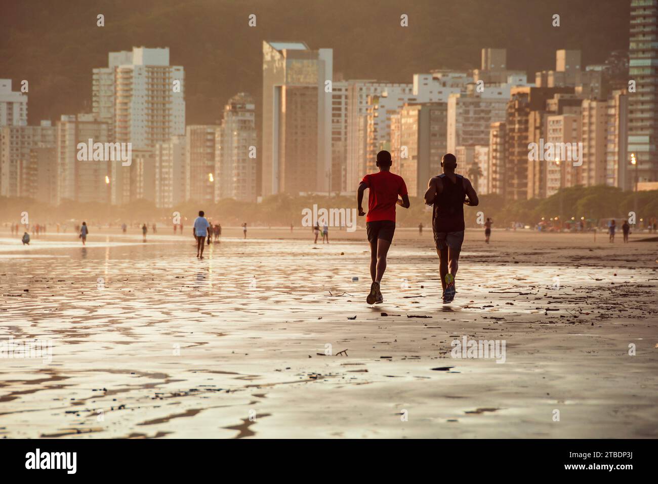 Two men running together on the beach at the golden afternoon in Santos ...