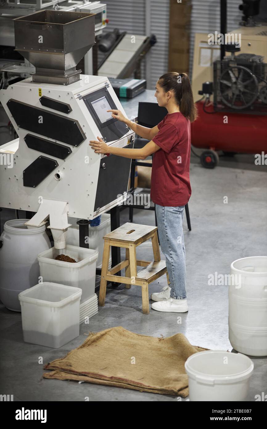 Vertical full length portrait of young woman operating machines at food ...