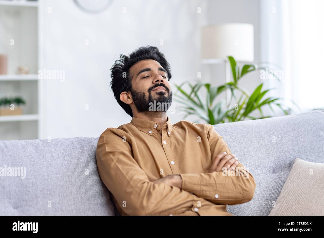 Tired young Indian man napping on couch at home with arms folded on ...