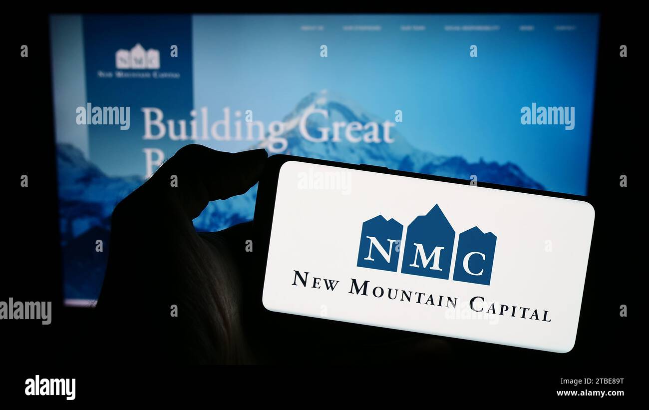 Person holding cellphone with logo of US investment company New Mountain Capital (NMC) in front ...