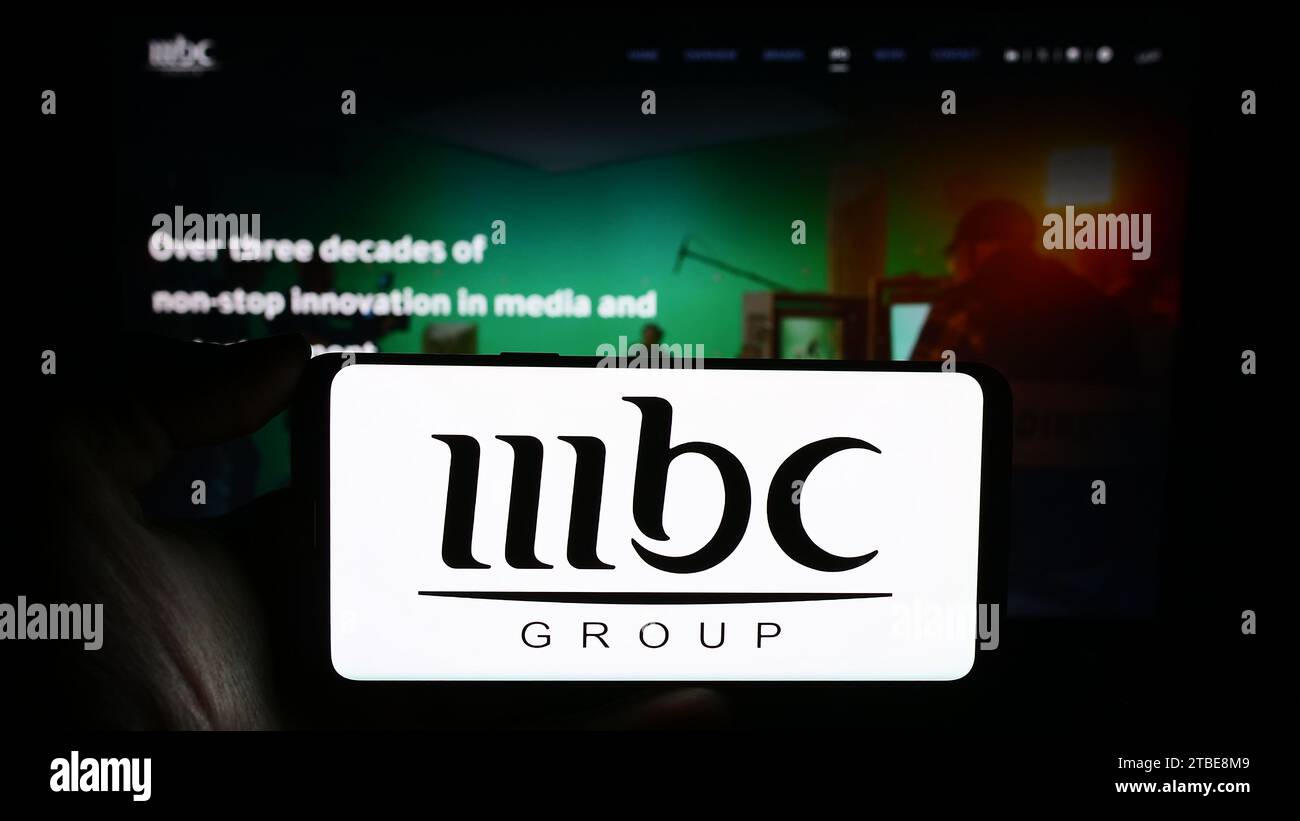 Person holding mobile phone with logo of Saudi Arabian media company MBC Group in front of ...
