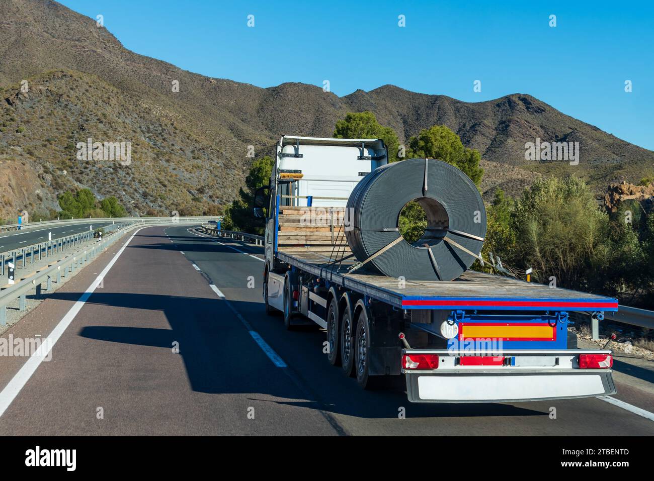 Truck with a hole in its trailer to transport a steel coil, held with ...