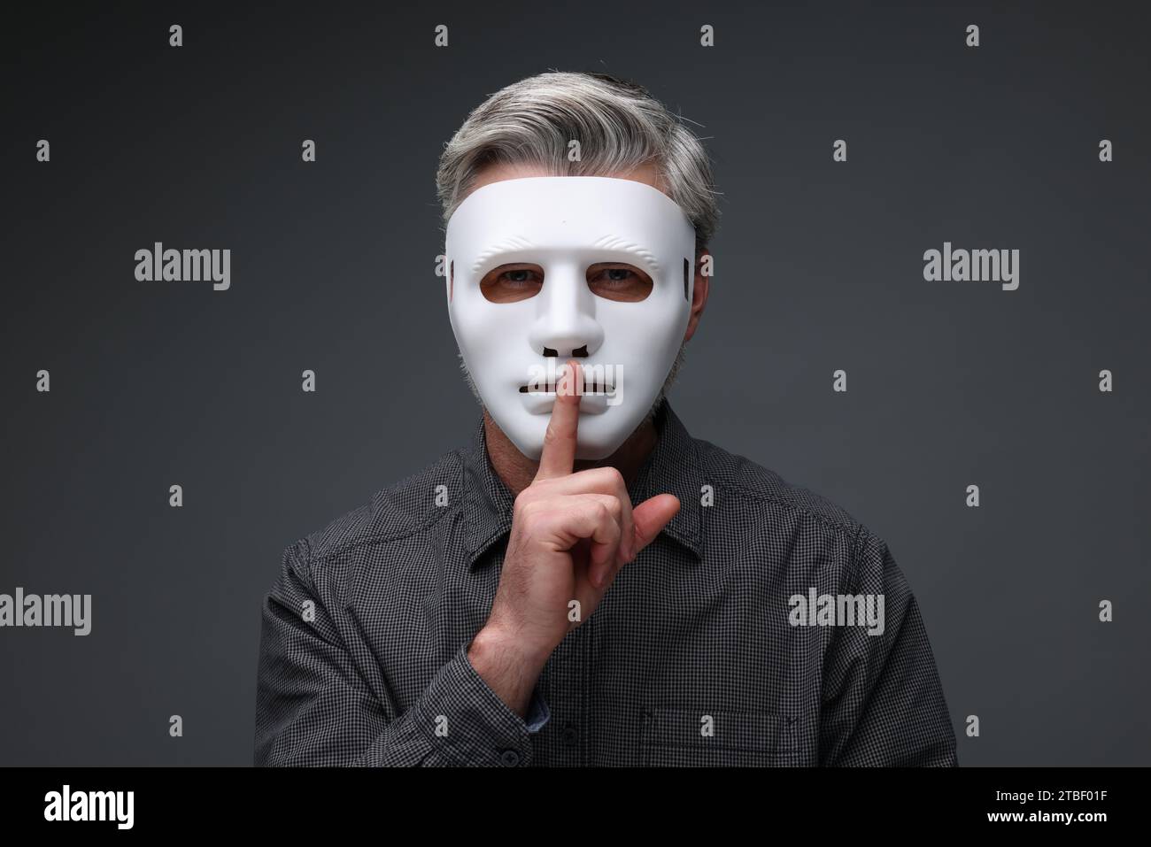 Man in mask showing hush gesture against dark grey background Stock ...
