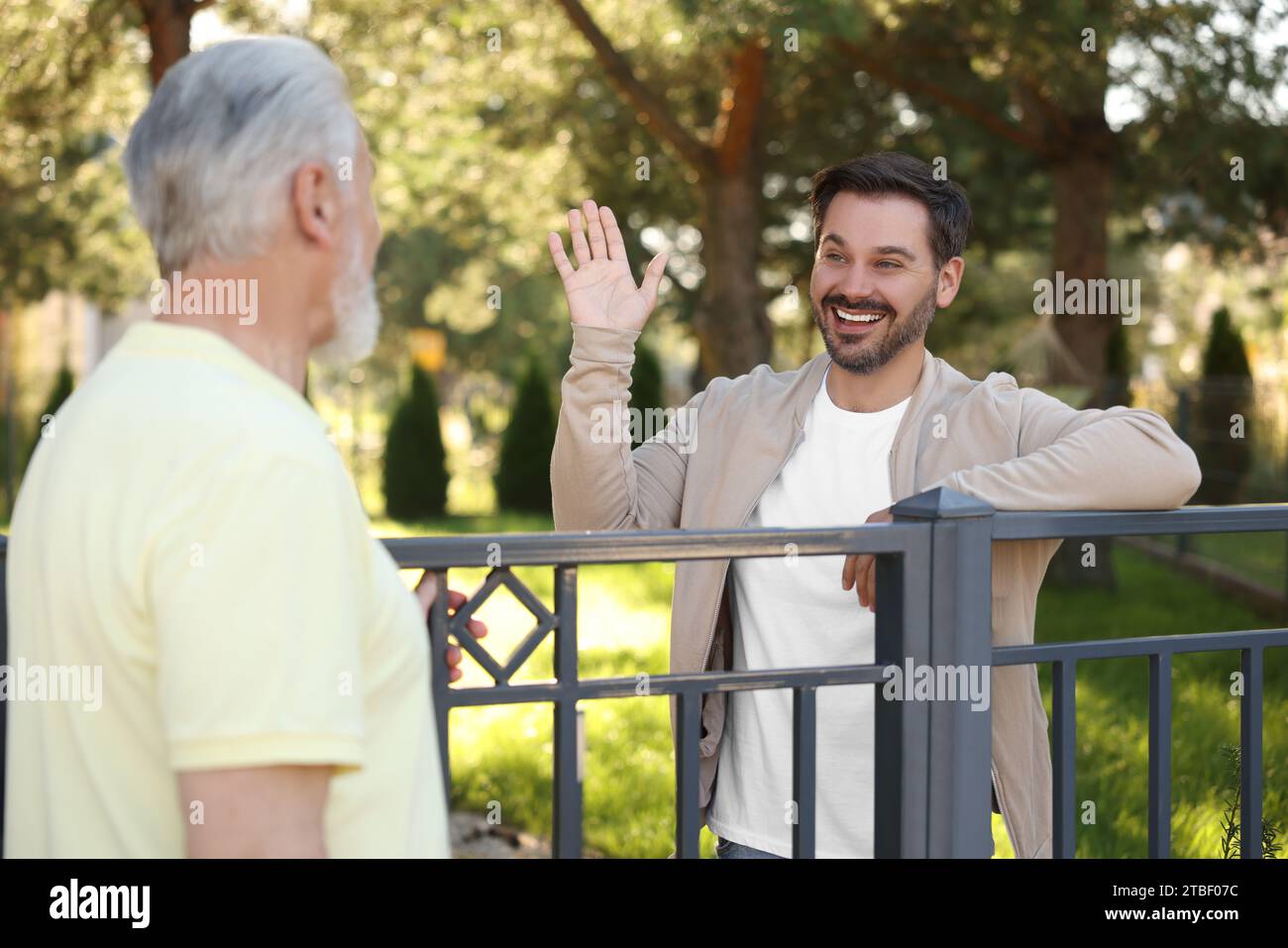 Friendly relationship with neighbours. Happy men near fence outdoors ...