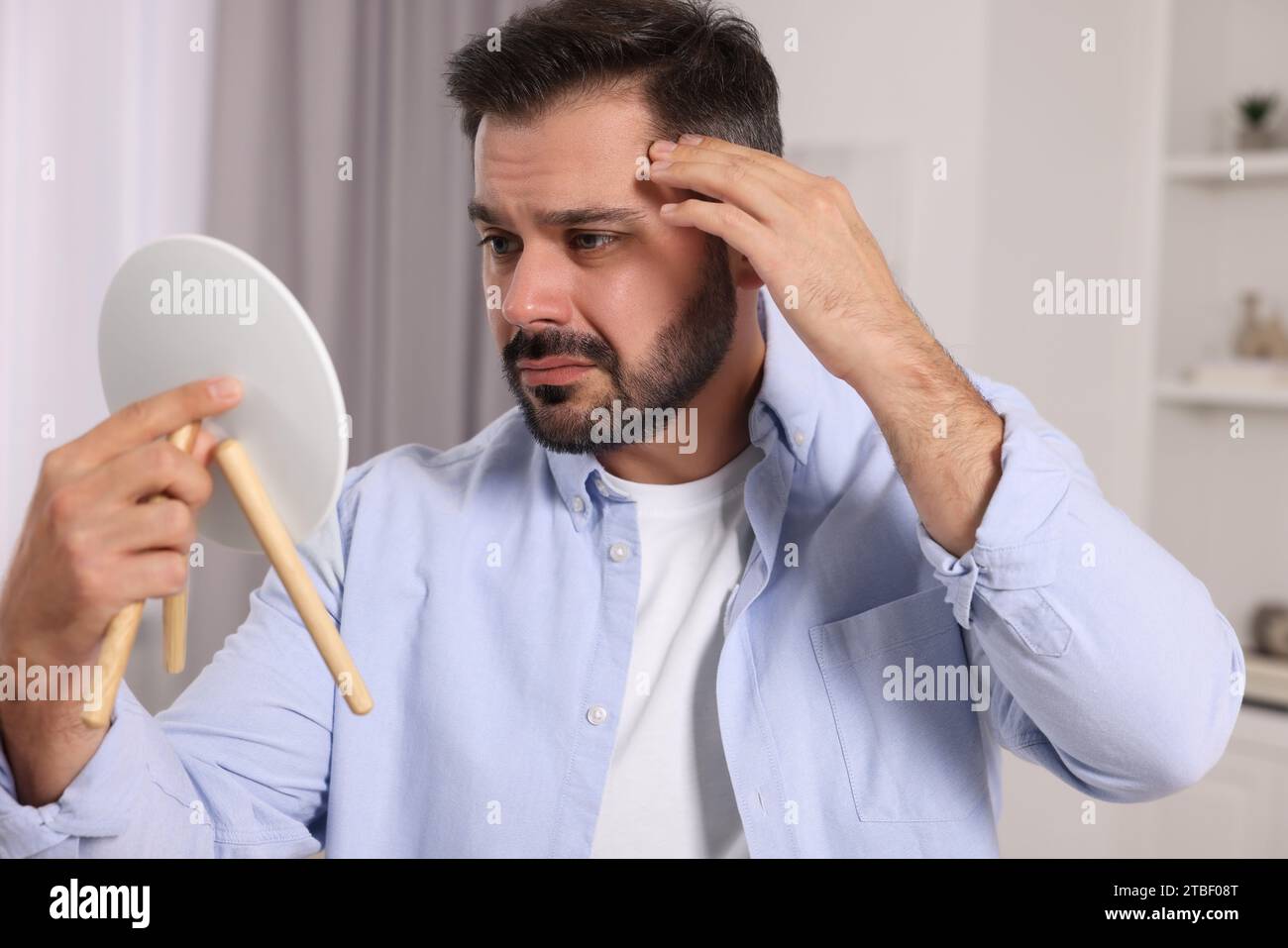 Confused man with skin problem looking in mirror at home Stock Photo ...