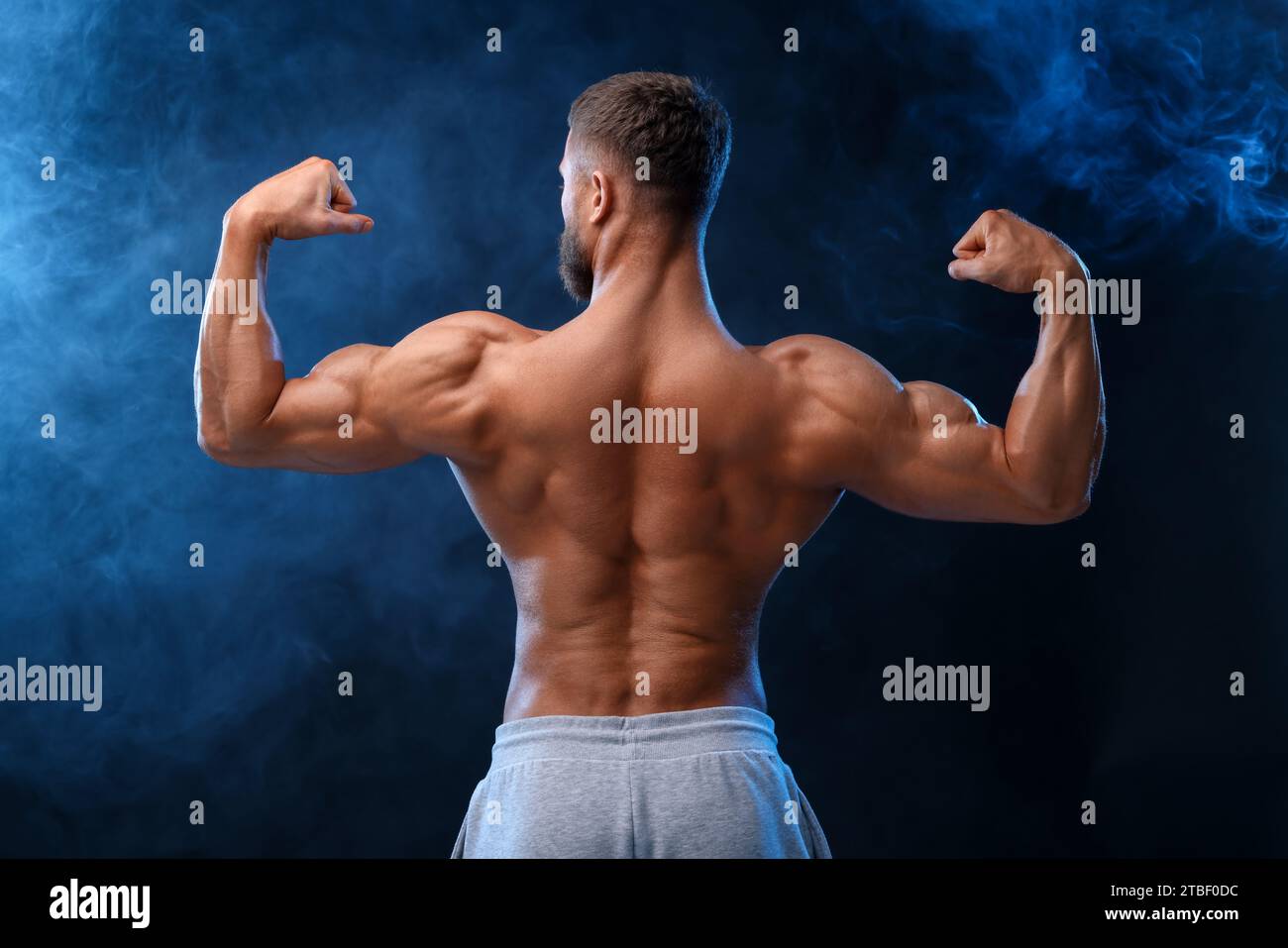 Young bodybuilder with muscular body in smoke on color background, back ...