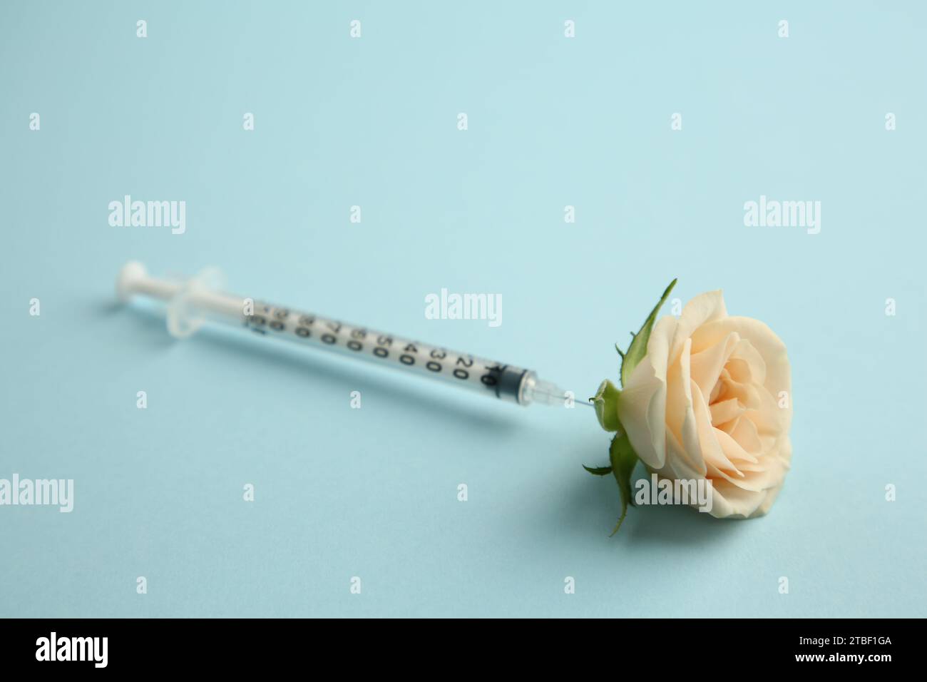 Medical syringe and beautiful rose on light blue background, closeup ...