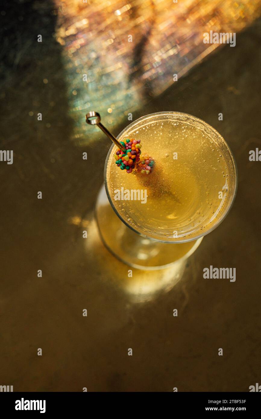 golden cocktail pick in glass of bubbly drink with colorful clusters of ...