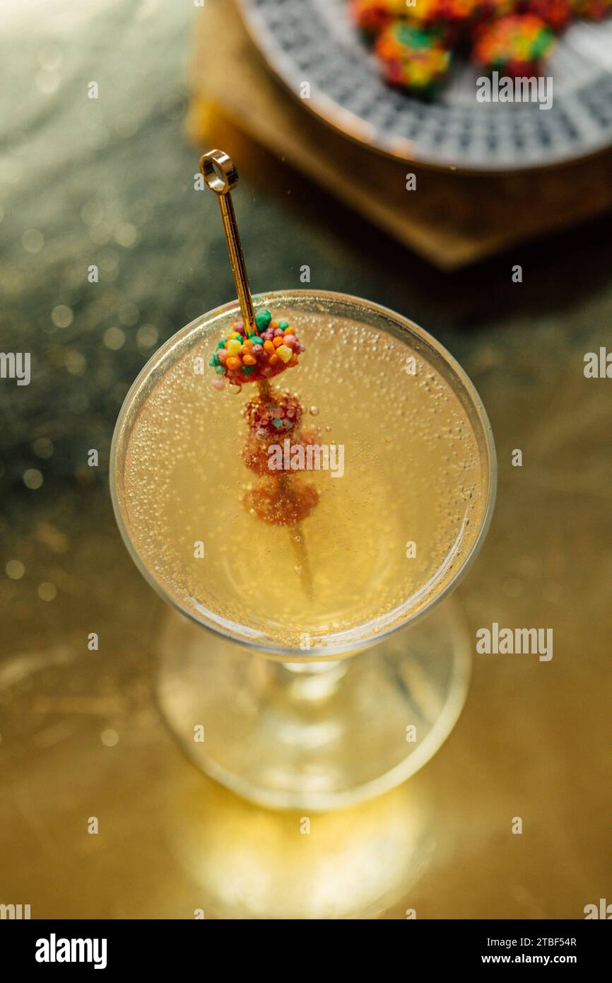 golden cocktail pick in glass of bubbly drink with colorful clusters of ...