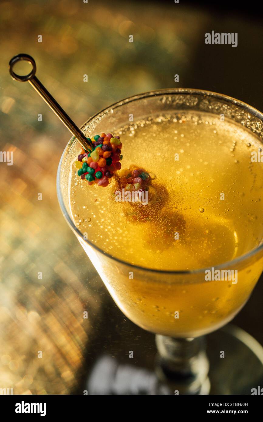 close up of golden cocktail pick in glass with colorful clusters of ...