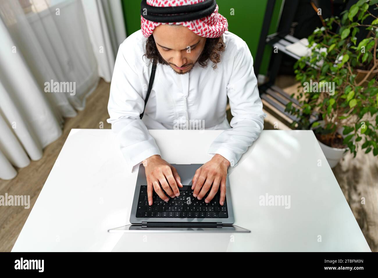 Young Arab man in traditional dress thobe working on computer in office ...