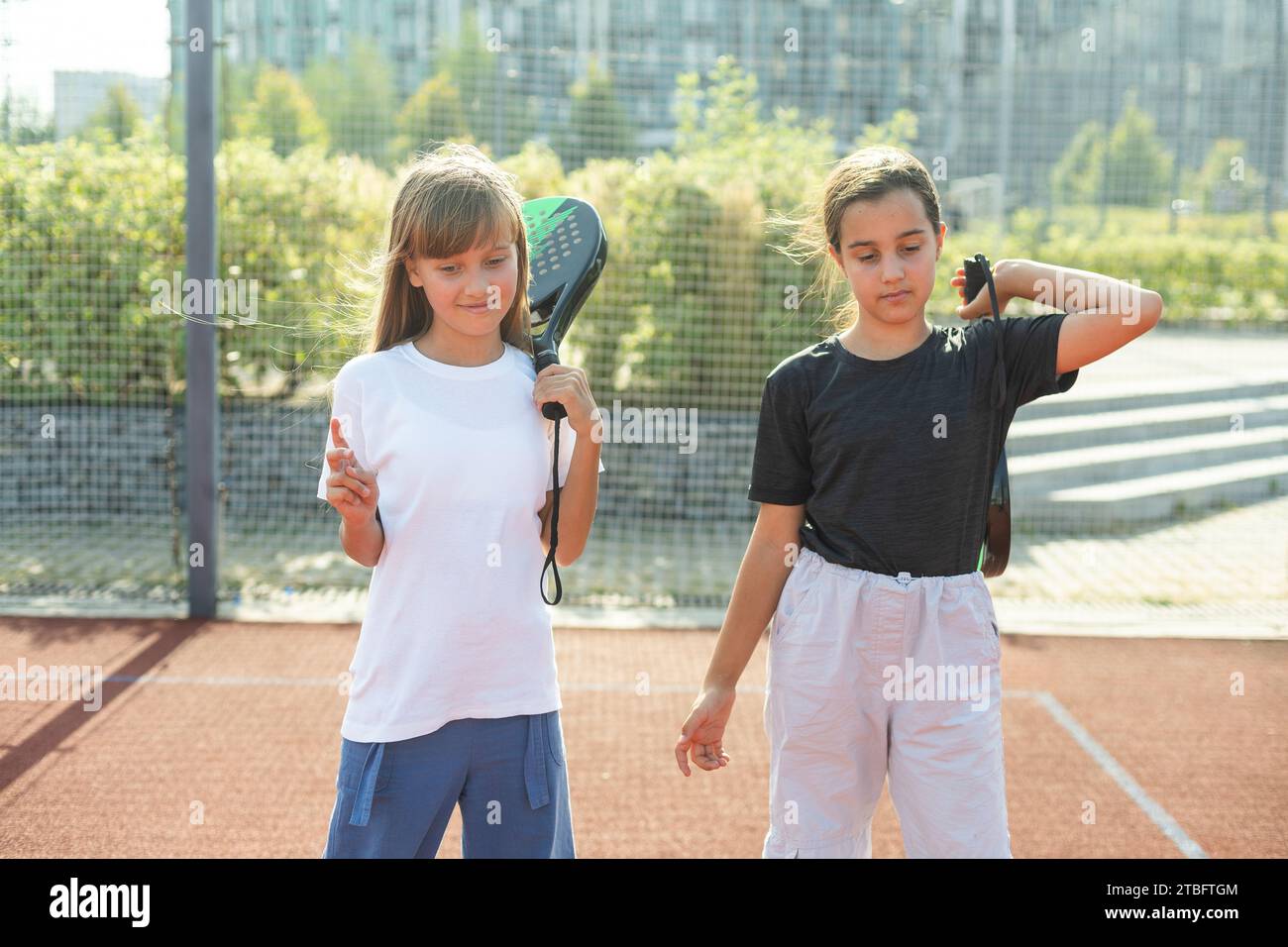Teenage girls with racquets and balls standing in padel court, looking ...