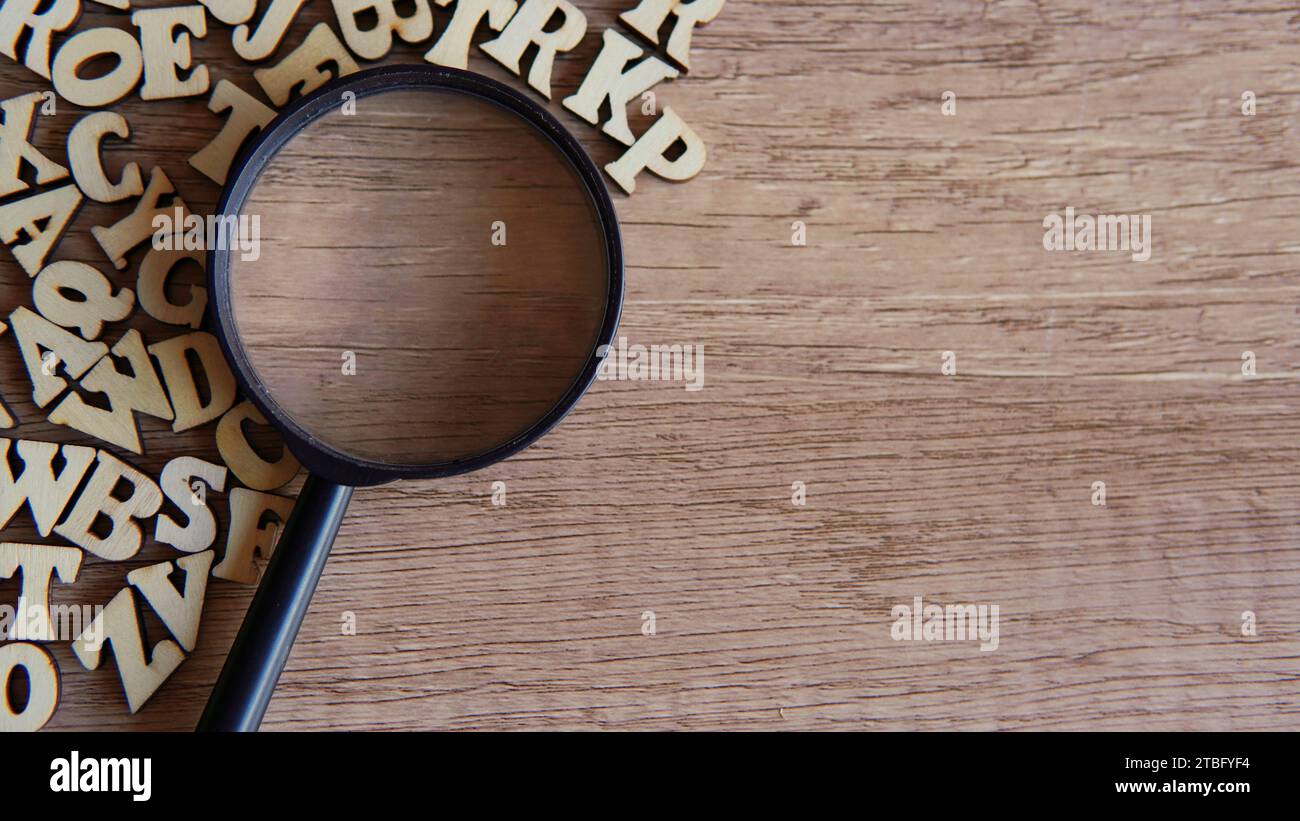 Magnifying glass with scattered alphabet letters on the table. Copy ...