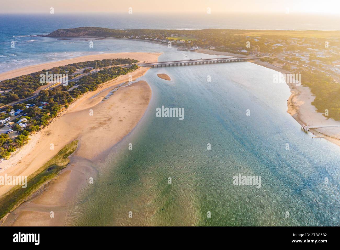 Aerial view of a wide river flowing out to sea under a bridge joining ...