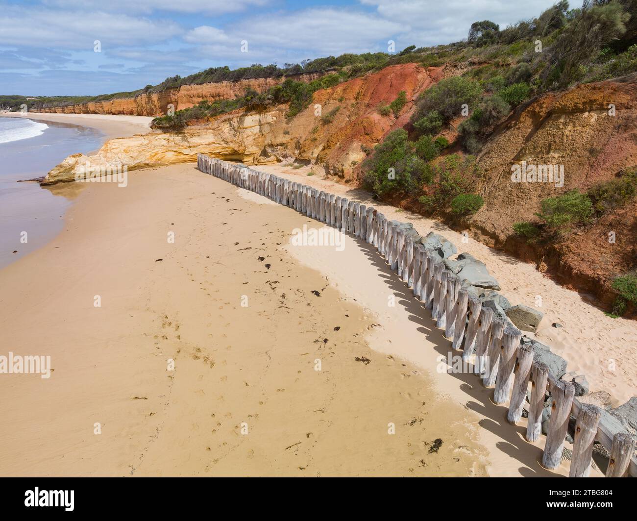 Aerial, view of a row of weathered bollards high on a sandy beach below ...