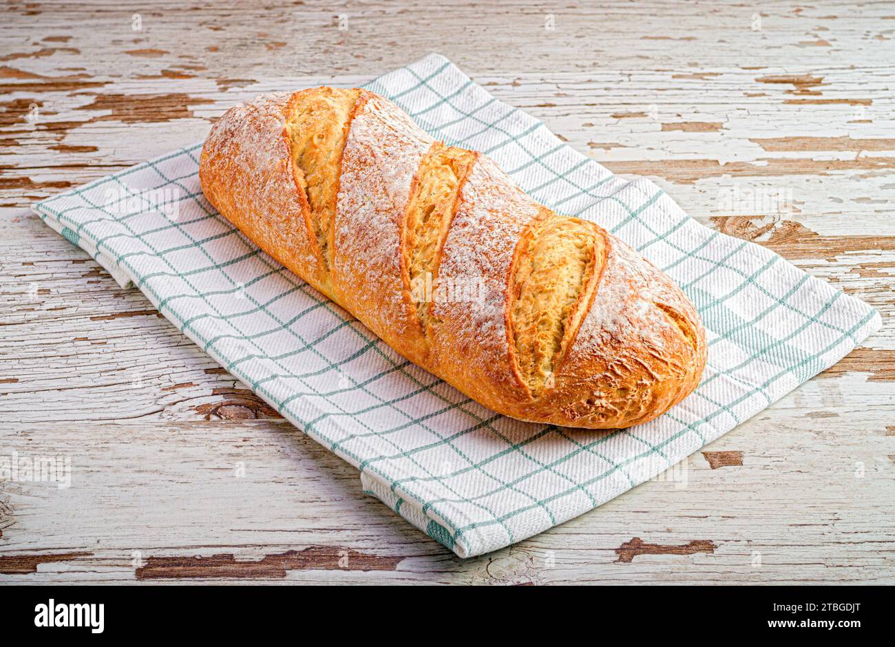 A freshly baked whole grain loaf of bread resting on a kitchen towel ...