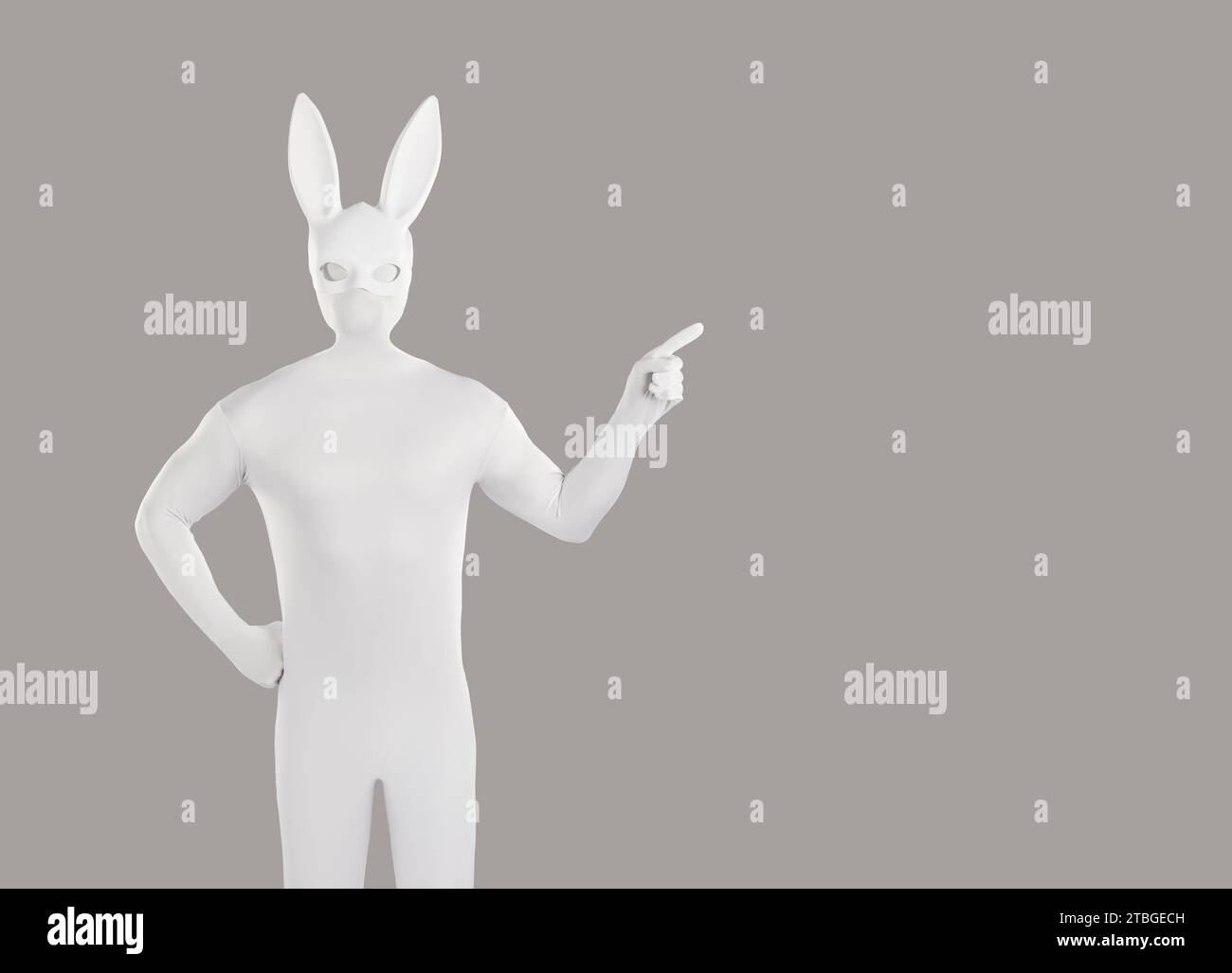 Man in white bodysuit and rabbit mask pointing to side on grey copy ...