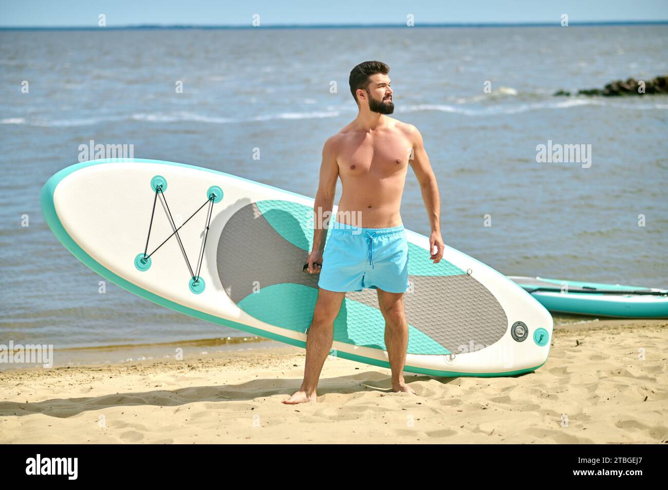 Man standing with paddle board on sandy beach near ocean , sup water ...