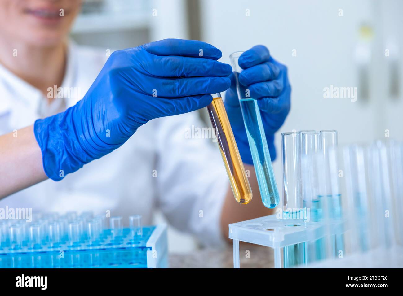 Woman biologist in lab coat and gloves holding test tubes with yellow ...