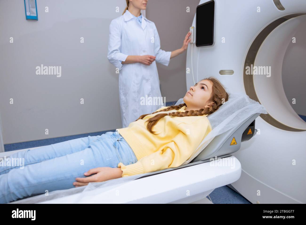 Little girl lying on table of mri scan machine while female ...