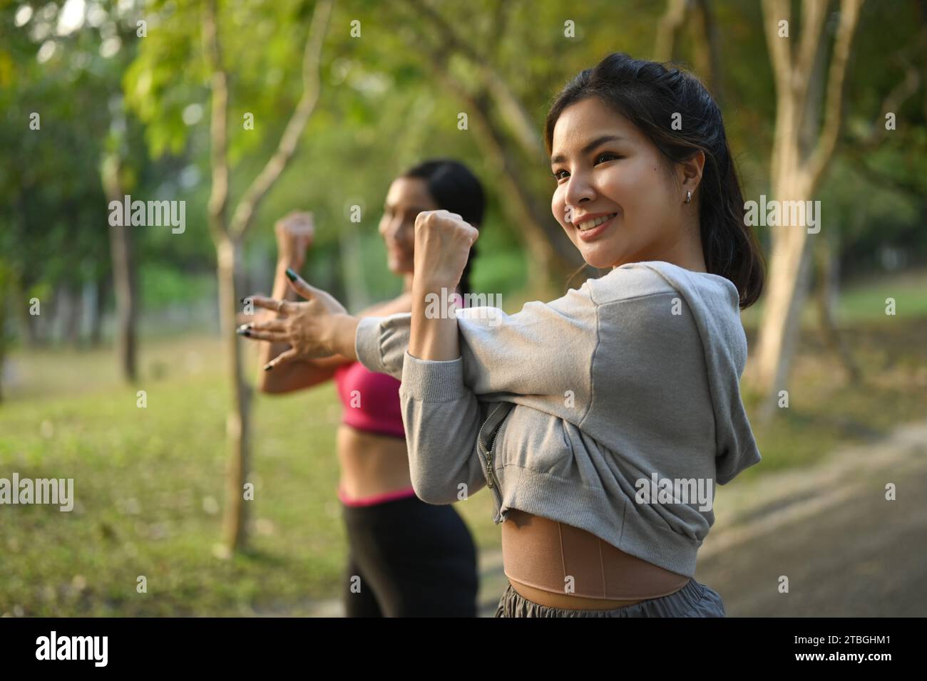 Two beautiful young sporty women doing stretching exercises before running in the summer park ...