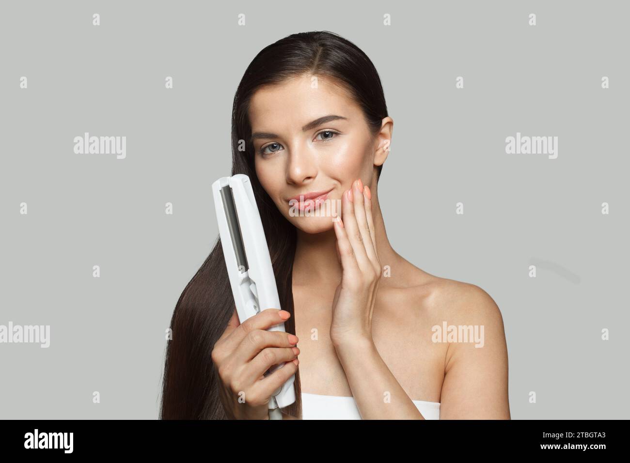Attractive woman using hair iron and straightening her long brown hair ...