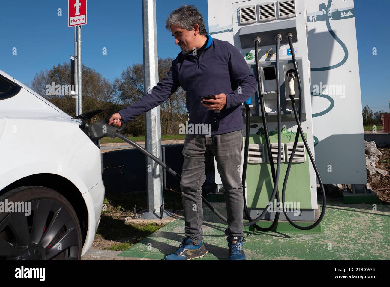Man pluggin in a CCS plug to his Tesla Model 3 electric car at a public ...