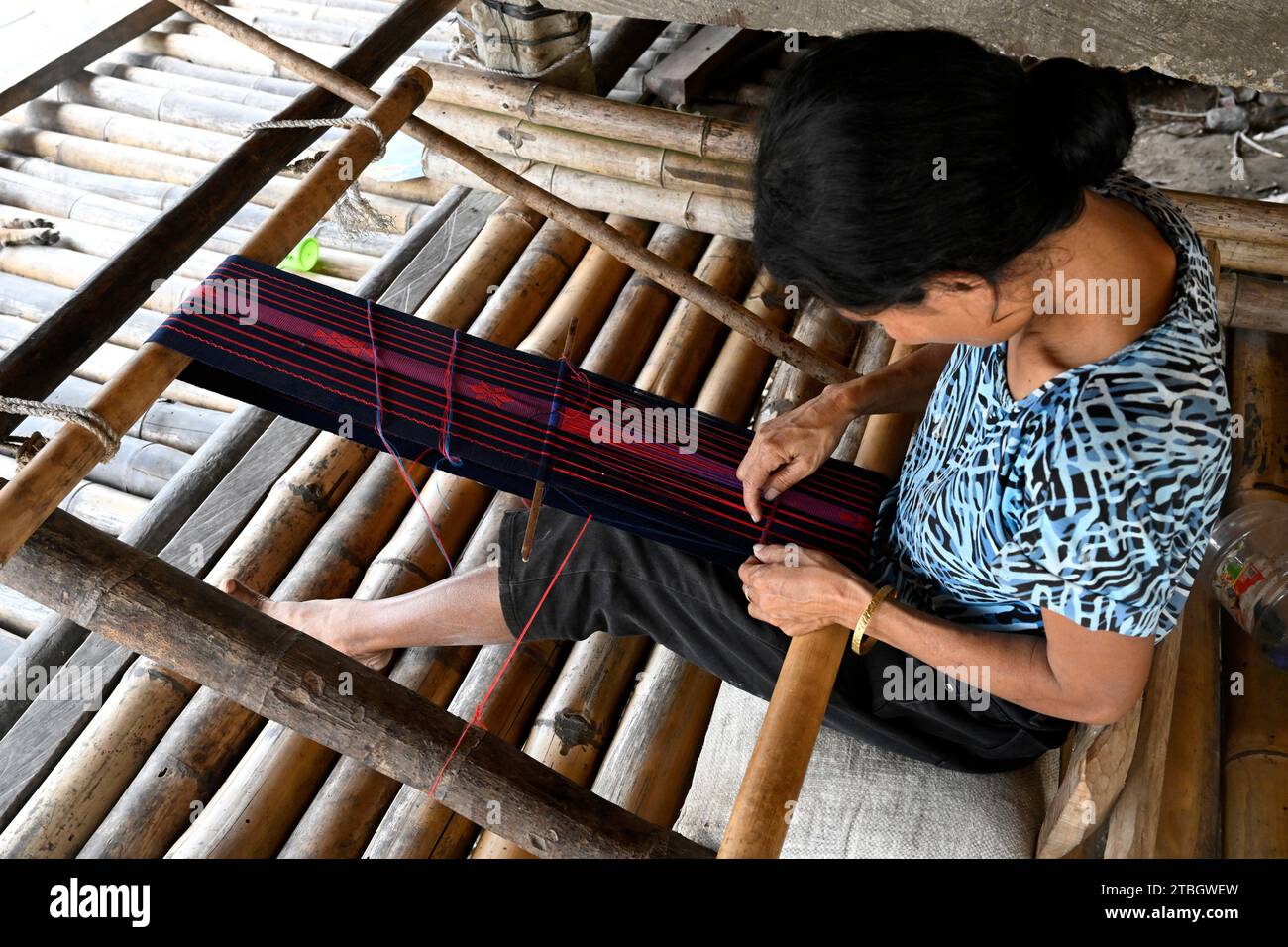 A woman sits at a traditional back strap hip loom weaving naturally ...