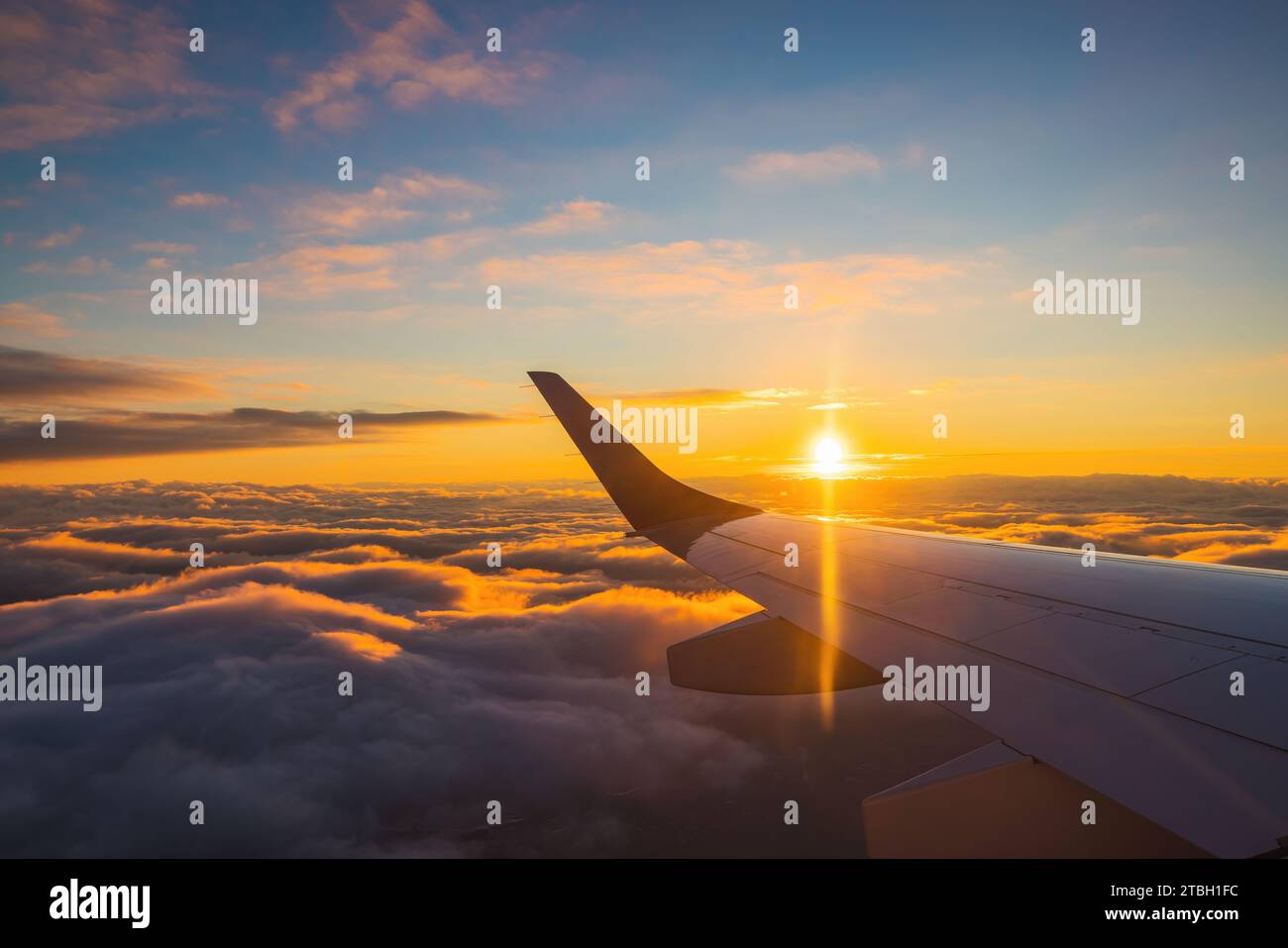 Airplane flight in sunset sky over ocean water and wing of plane. View ...