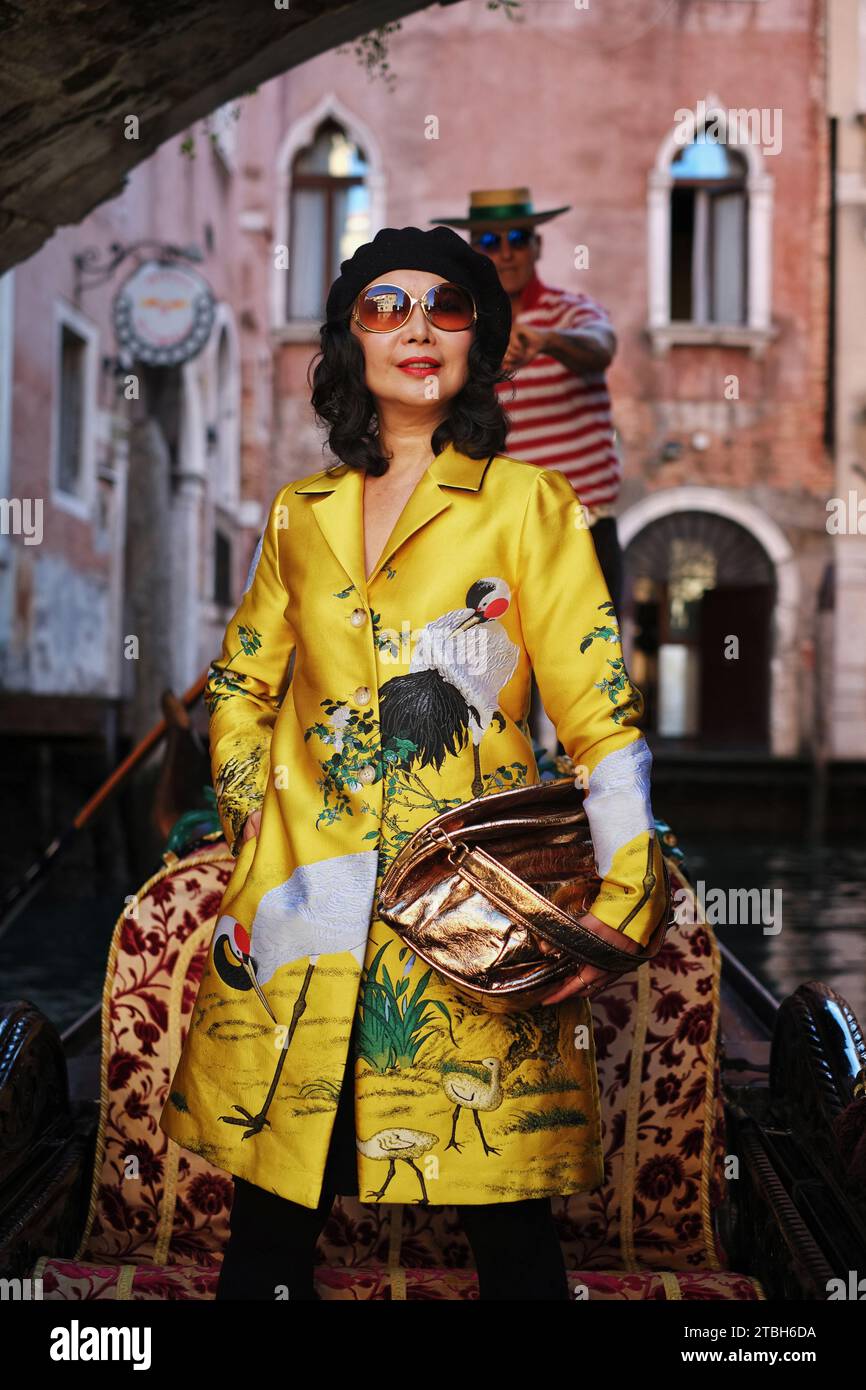 Venice, Italy, a glamorous woman standing in a gondola wearing a gold ...