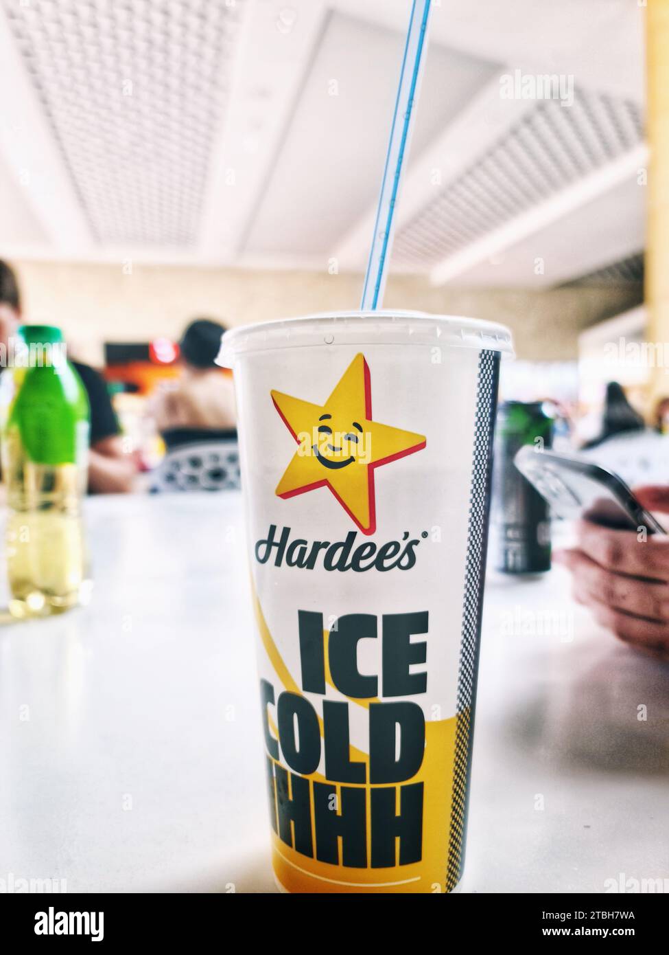 A paper cup branded Hardees stands on a table in the food court area ...