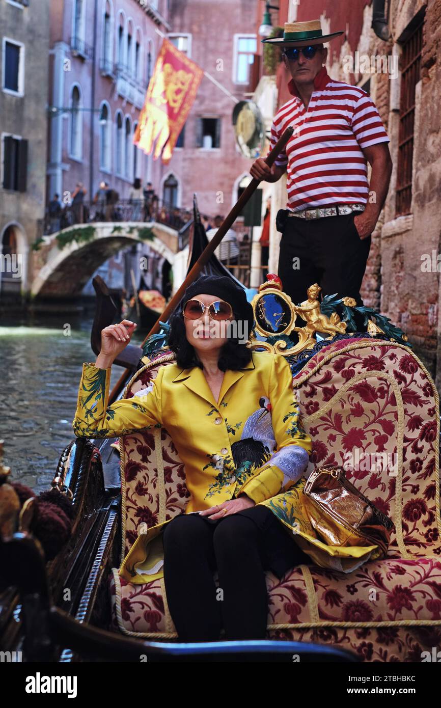 Asian woman wearing a golden coat sitting in a gondola being rowed by a ...