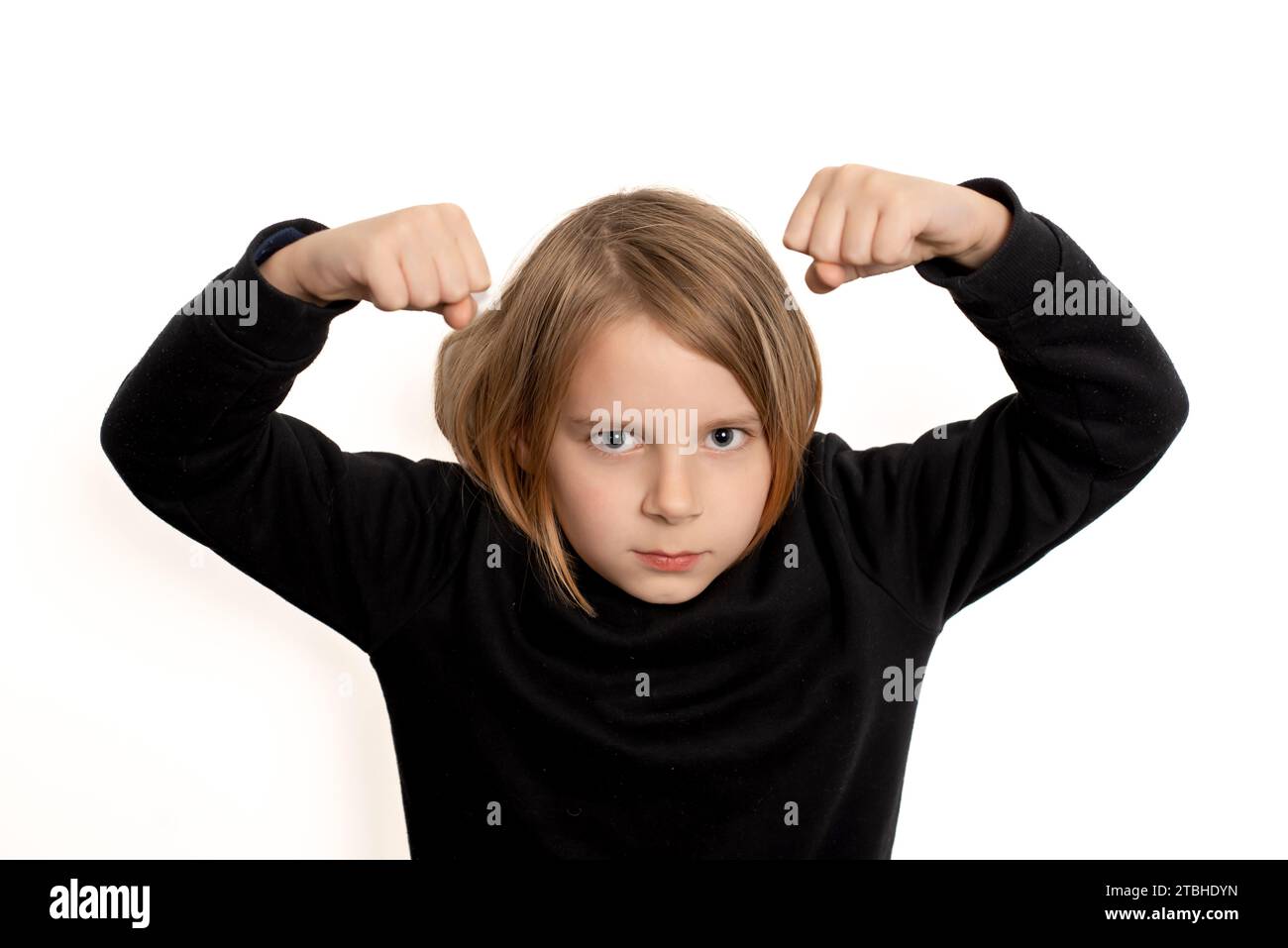 A young boy with long hair demonstrates strength by flexing his arms in ...