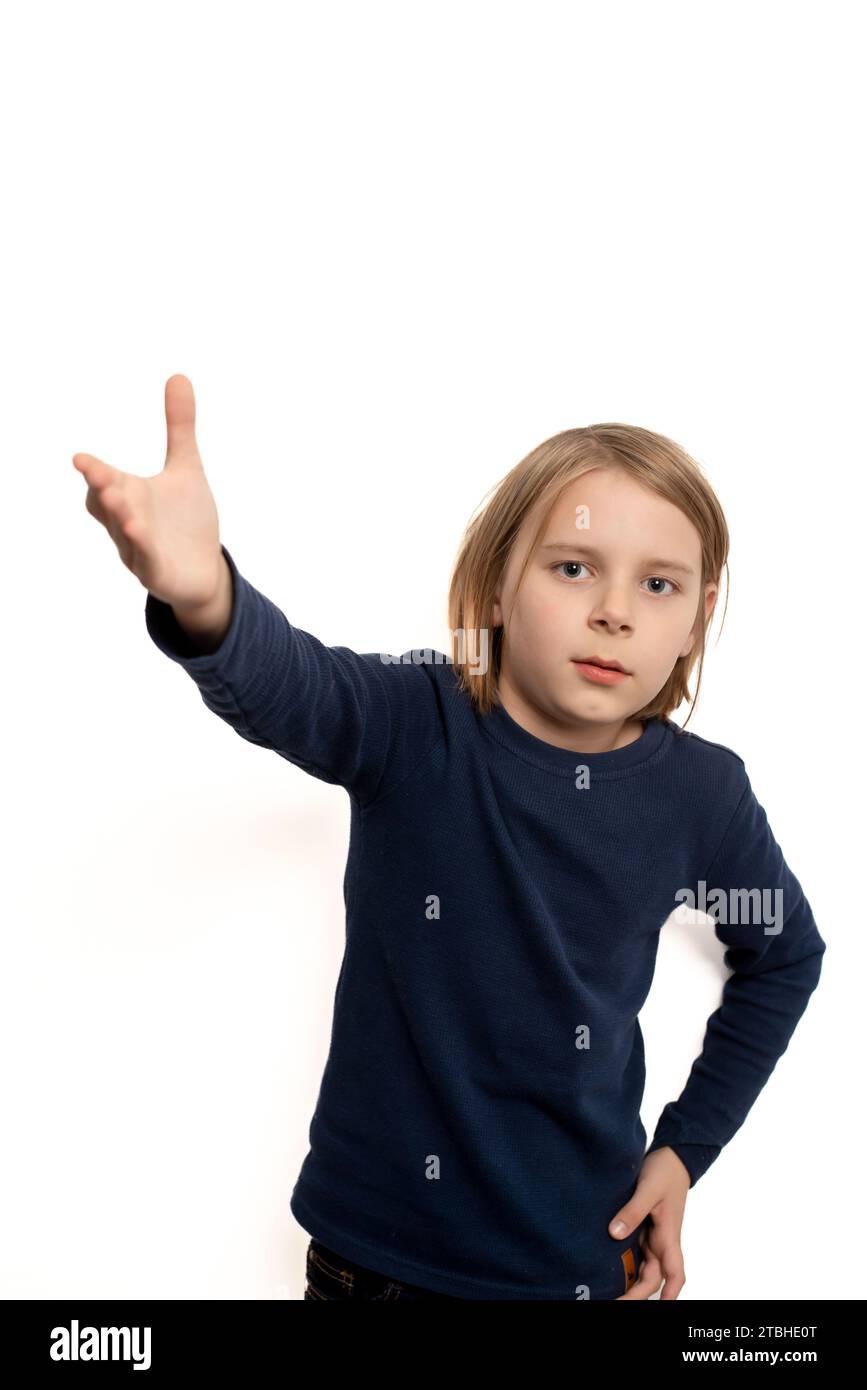 A young boy with long hair points towards the camera, creating a direct ...