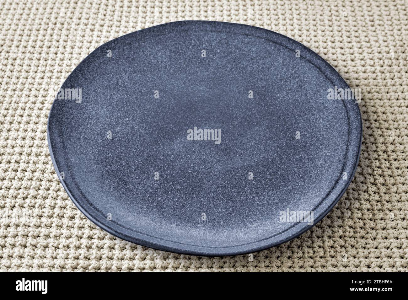 Gray ceramic plate of irregular shape on a beige knitted background ...