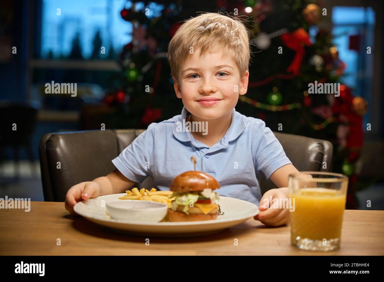 Cute boy eating burger while sitting in restaurant during winter ...