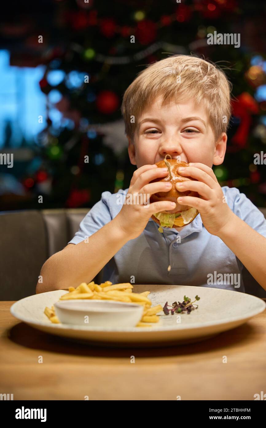 Little boy biting sandwich in festive restaurant sitting New Year ...
