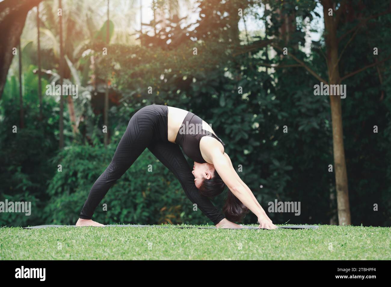 Asian woman practicing yoga in Intense Side Stretch Pose on the mat in outdoor park Stock Photo ...