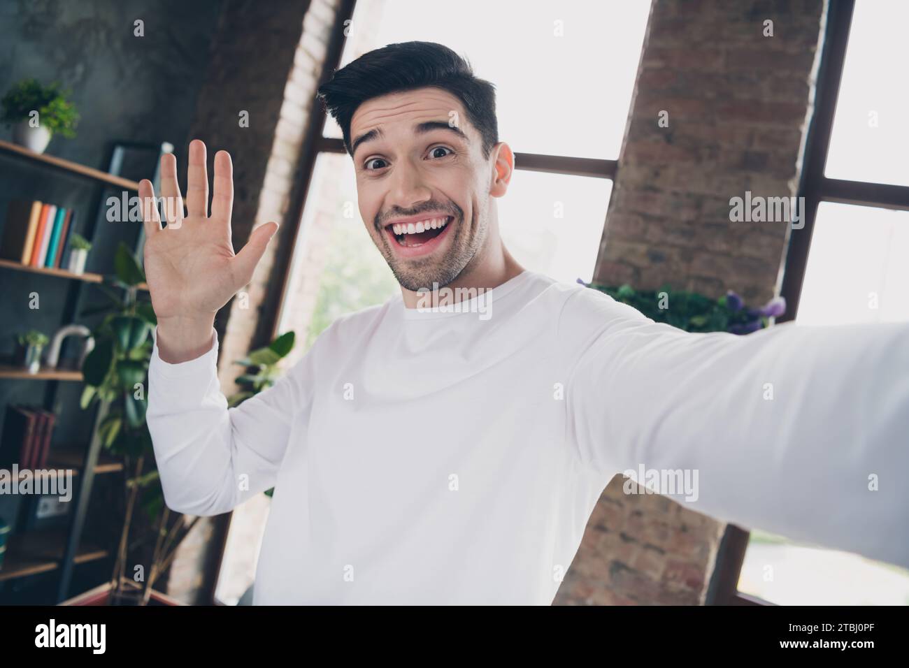 Photo of good mood friendly young guy dressed white shirt waving arm hi ...