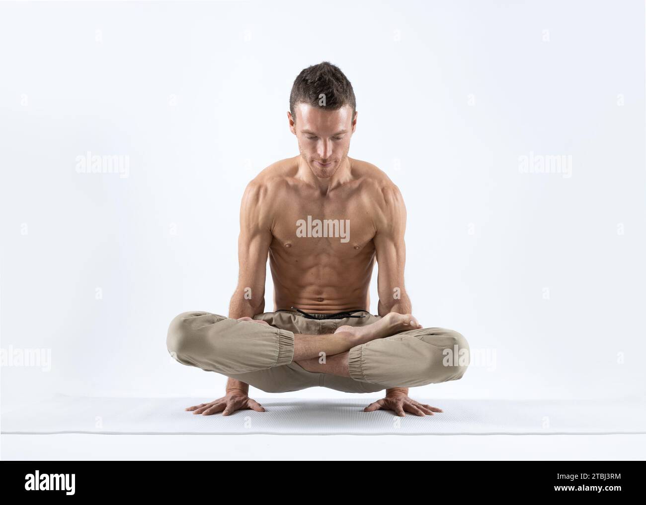 advanced male yogi doing tolasana (scale pose) on a white mat with a ...