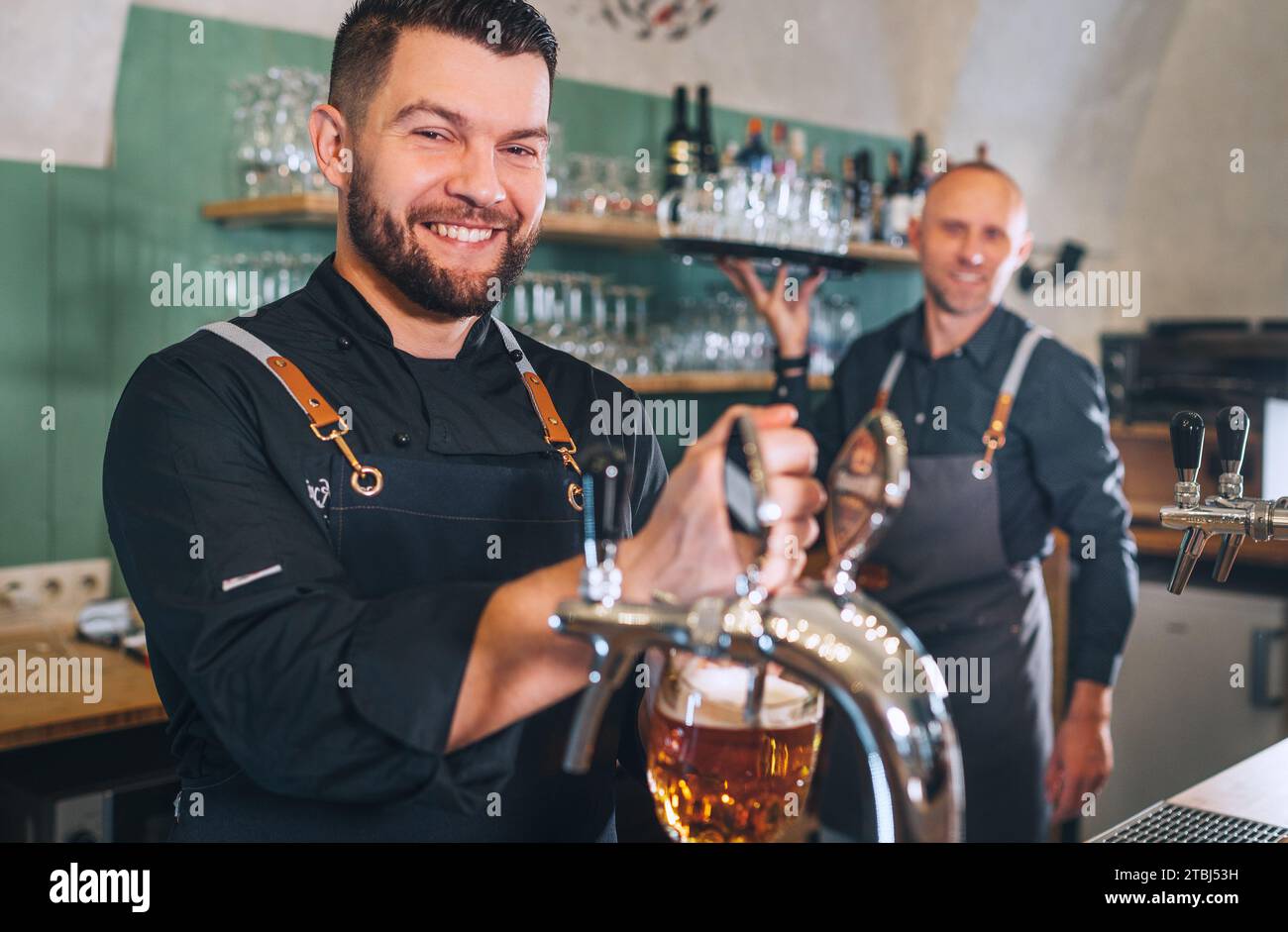 Stylish bearded barman dressed black uniform smiling at camera, beer ...