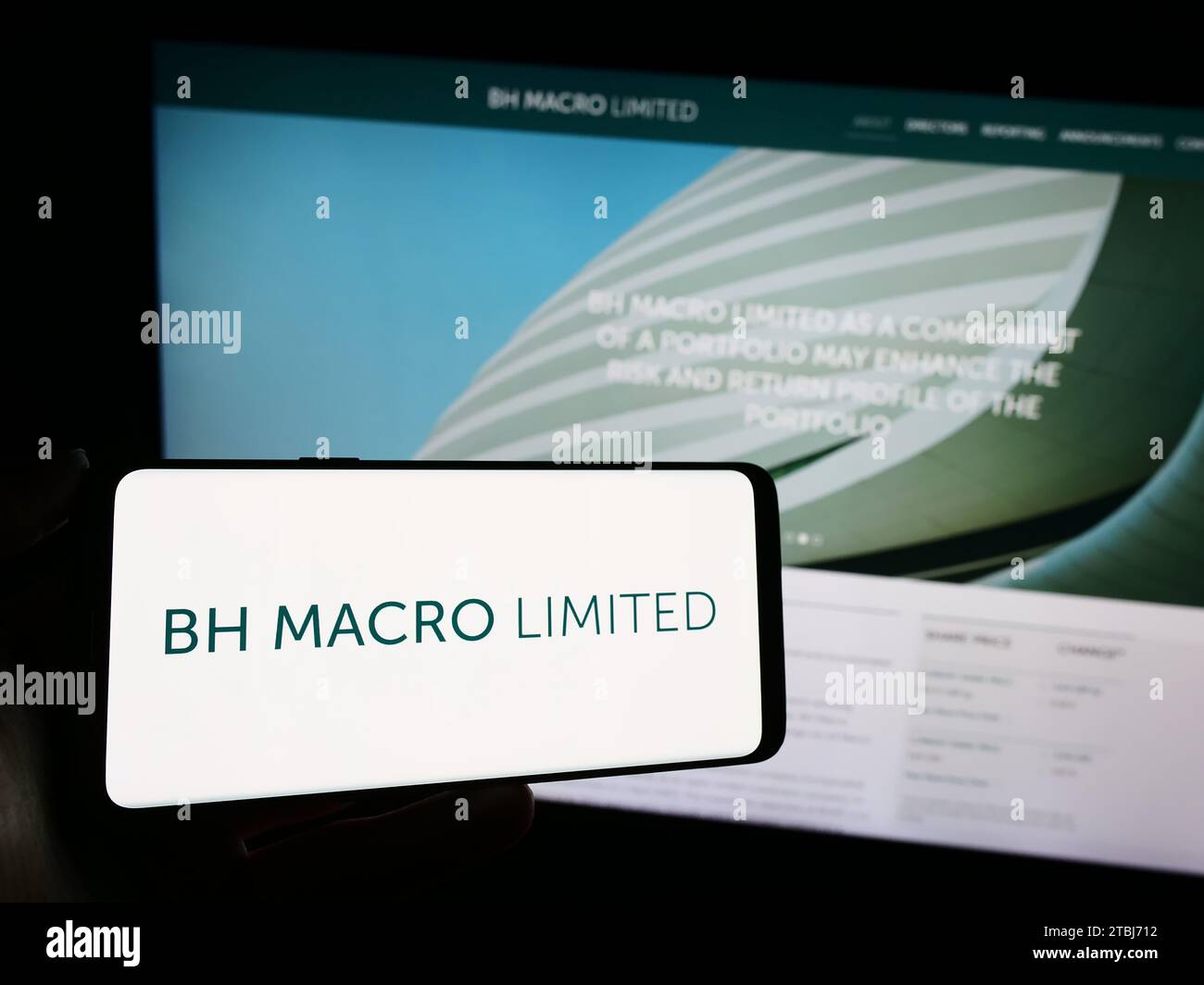 Person holding cellphone with logo of investment company BH Macro Limited in front of business ...