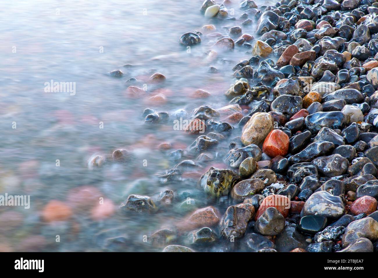 Blurred sea water of wave rolling over wet colourful pebbles on shingle ...