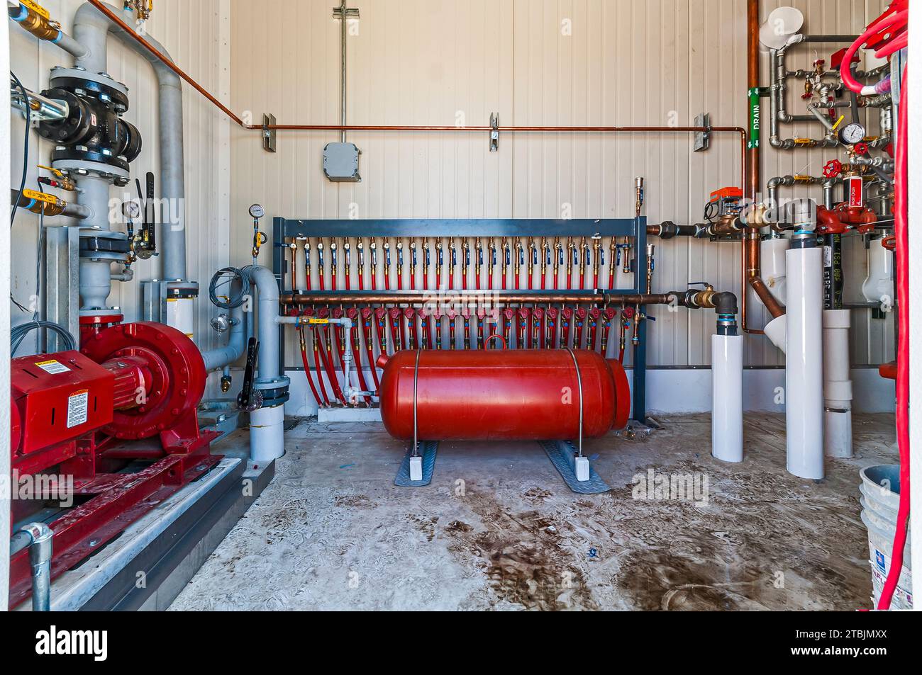 A rack of valves, red hoses, and a red tank in a small control room on ...