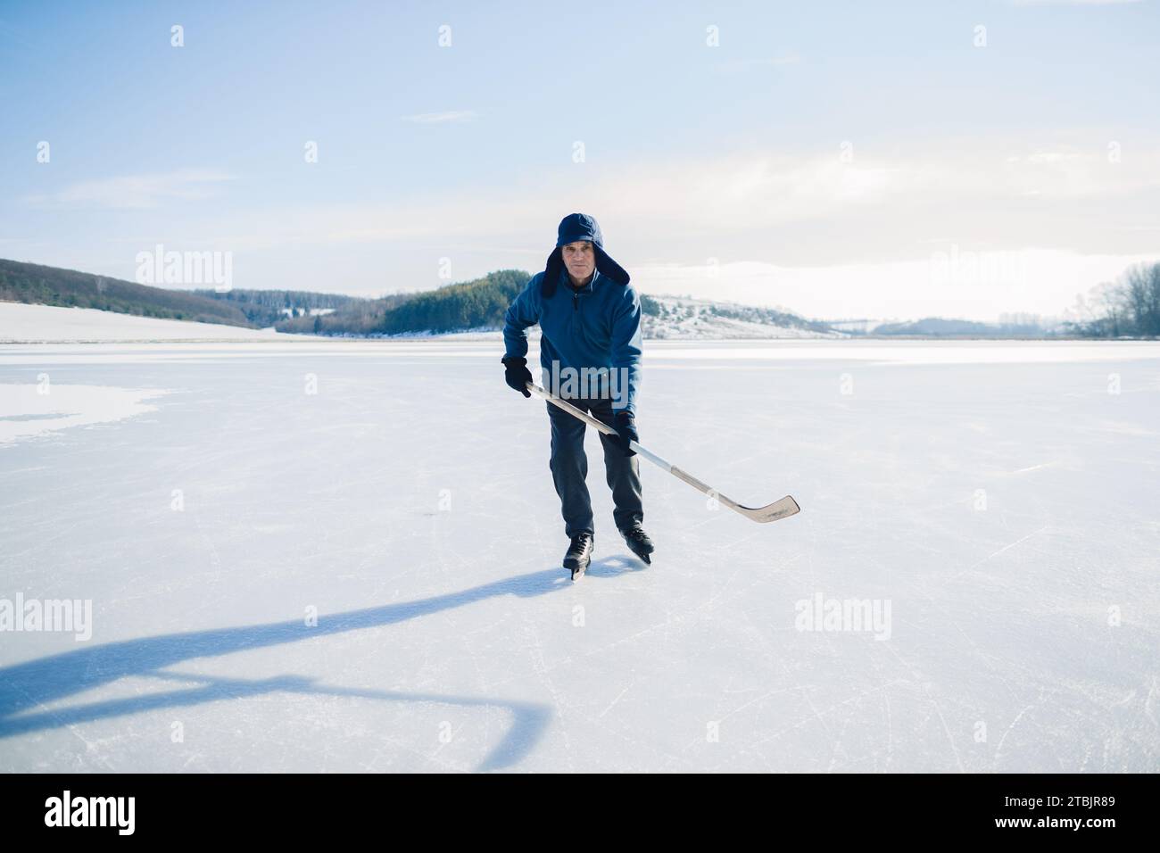Senior man with hockey stick skating on ice in winter. Looking into the ...