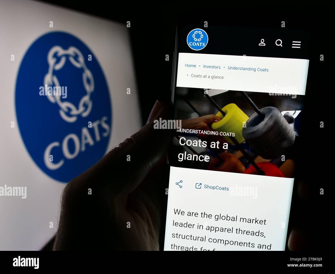 Person holding cellphone with webpage of British textile material company Coats Group plc in ...