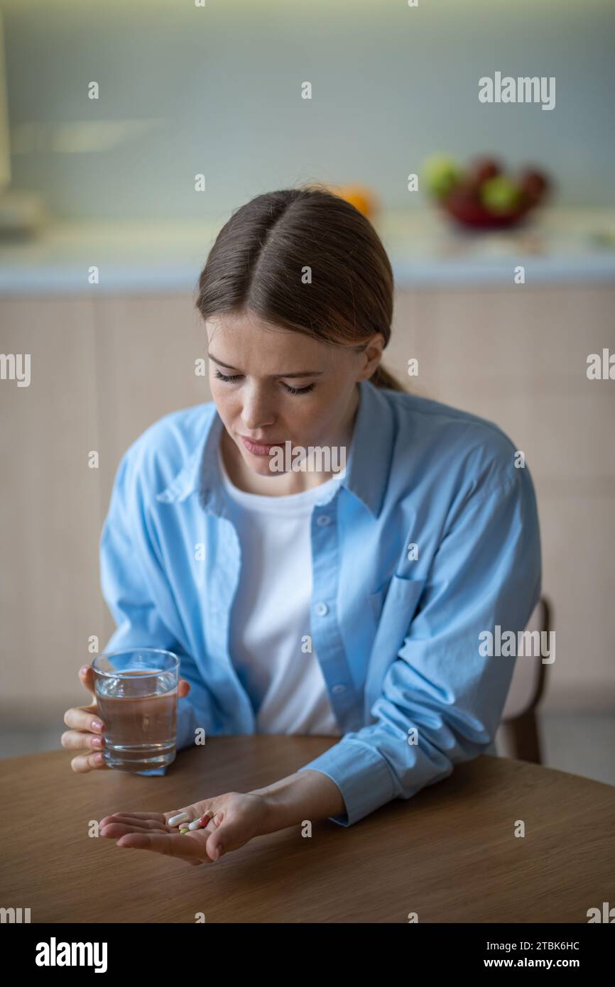 Stressed unhealthy woman holding capsules, glass of water, suffering ...