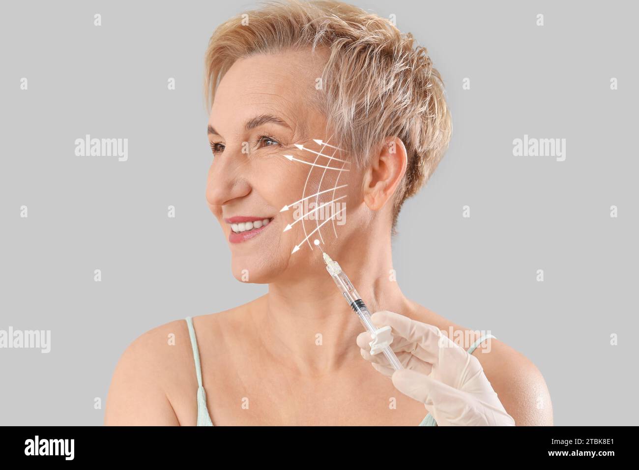 Mature woman receiving filler injection in face against light ...