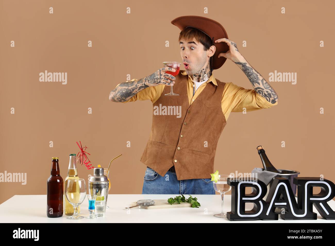 Shocked male bartender dressed as cowboy with glass of cocktail at ...